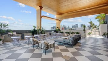 Terraço no telhado com área de estar ao ar livre, churrasqueira e vista para o horizonte da cidade.
