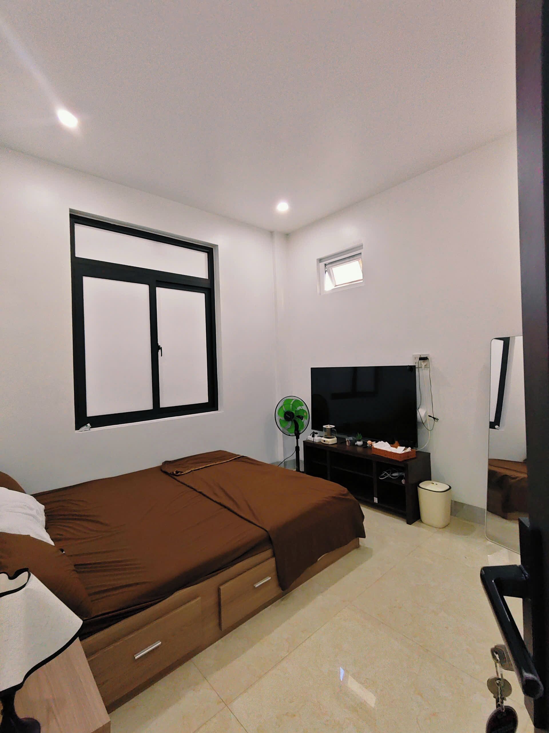 Quarto com cama, televisão, ventoinha e uma pequena janela.