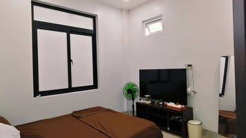 Quarto com cama, televisão, ventoinha e uma pequena janela.