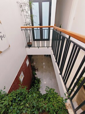 Interior com vários níveis, uma escada, corrimão de madeira e vista para uma porta com painéis de vidro jateado.