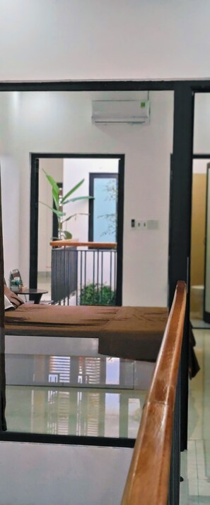 Quarto com mesa de vidro, um banco de madeira, uma planta em vaso e vista para uma varanda com corrimão.