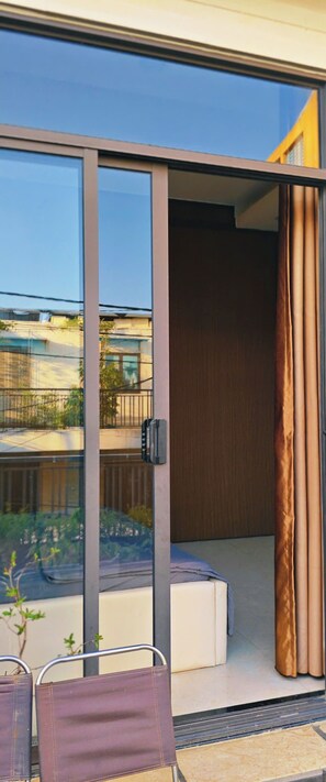 Uma porta de correr moderna de vidro que dá para uma varanda com área de estar acolchoada e vista dos edifícios ao redor.