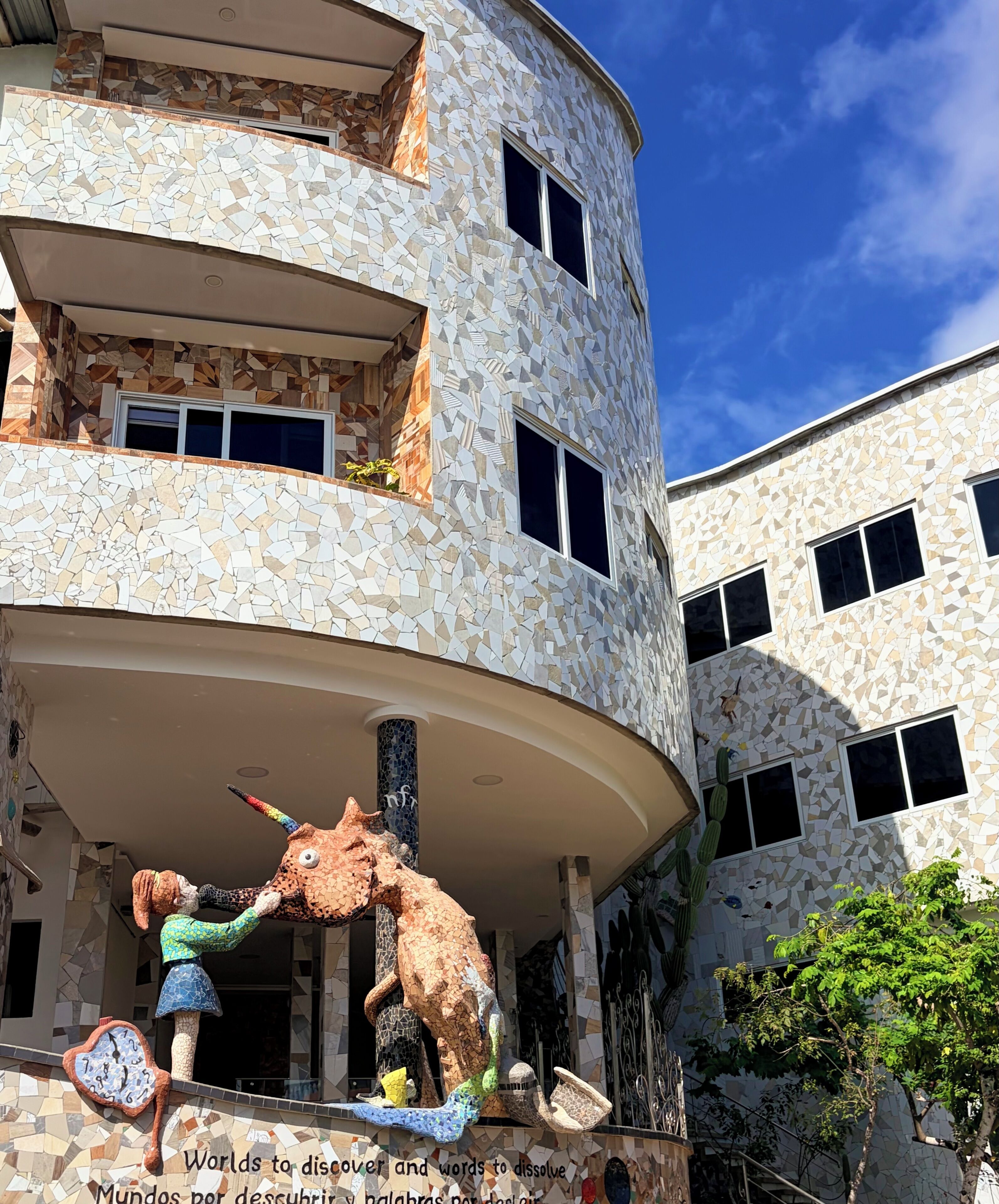 Um edifício de vários andares com fachada em mosaico e uma escultura de um dinossauro e uma figura humana.