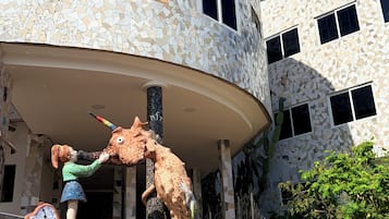 Um edifício de vários andares com fachada em mosaico e uma escultura de um dinossauro e uma figura humana.