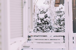 Varanda coberta de neve, com corrimão branco e um banco.