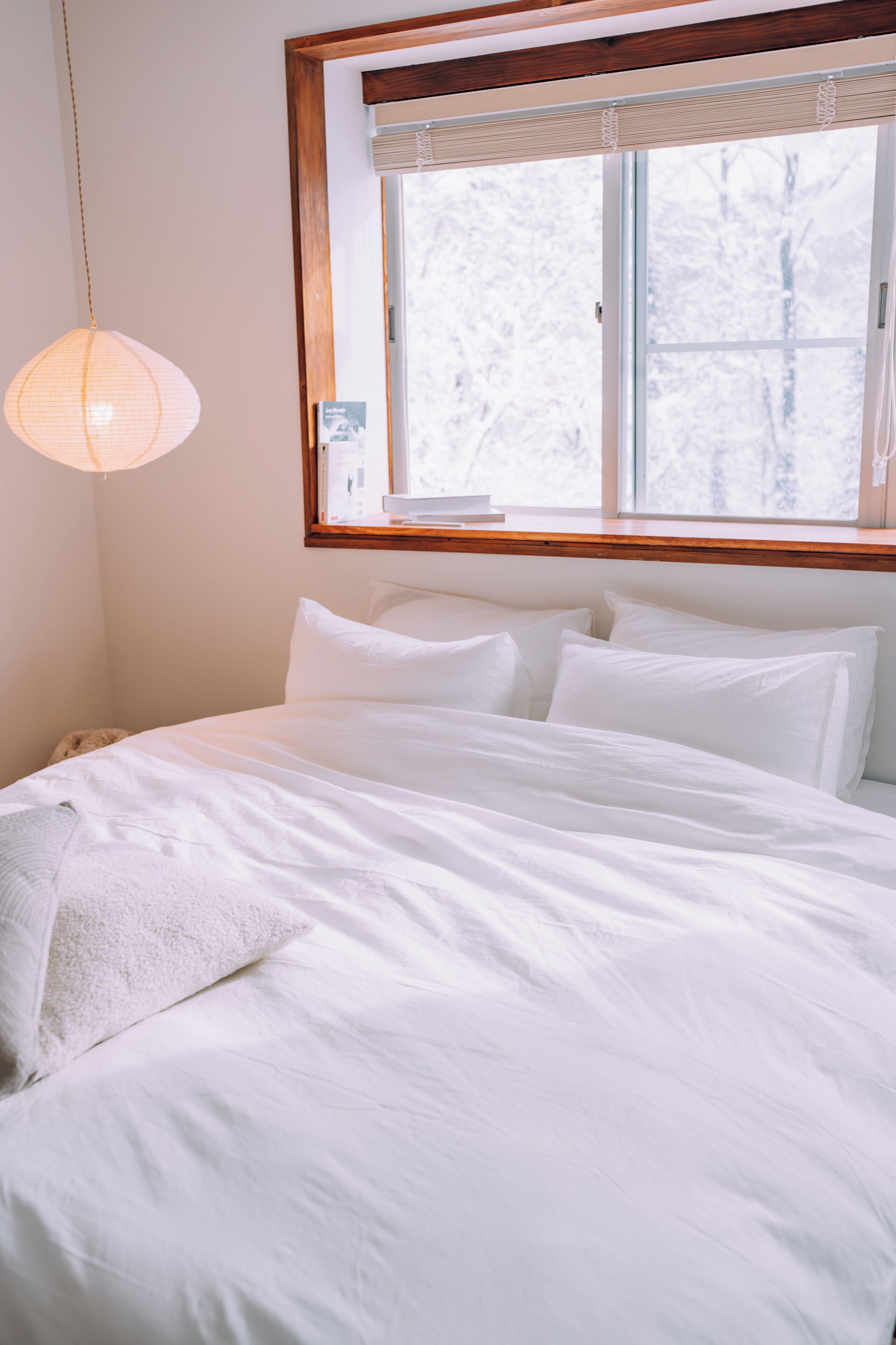 Quarto com uma cama, luminária pendente e janela com vista para árvores.
