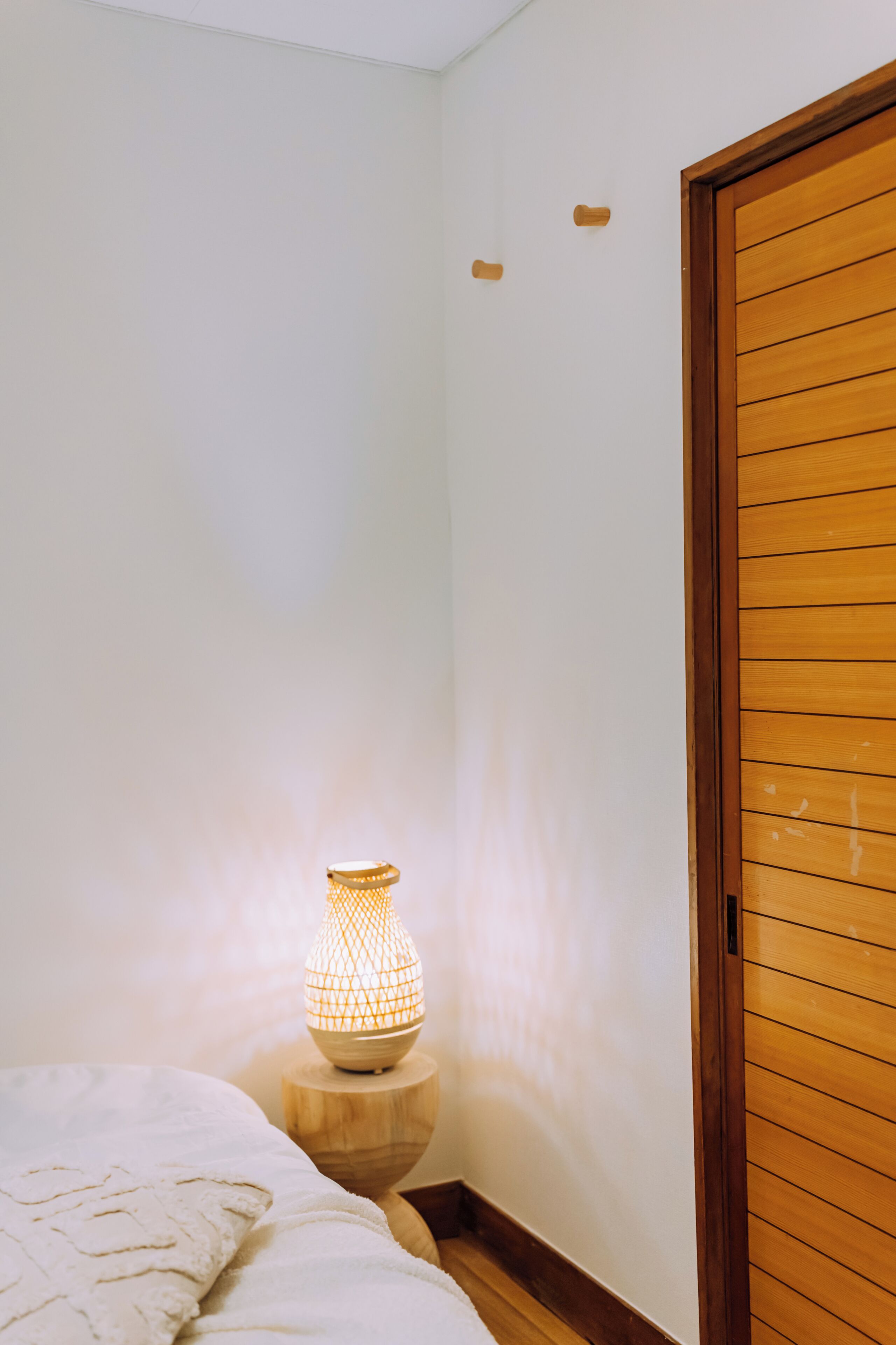 Quarto com cama, mesa de cabeceira com abajur e guarda-roupa de madeira.