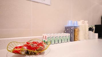 Uma bancada de cozinha com uma cesta de biscoitos, pilhas de caixas de leite e uma fileira de copos descartáveis.