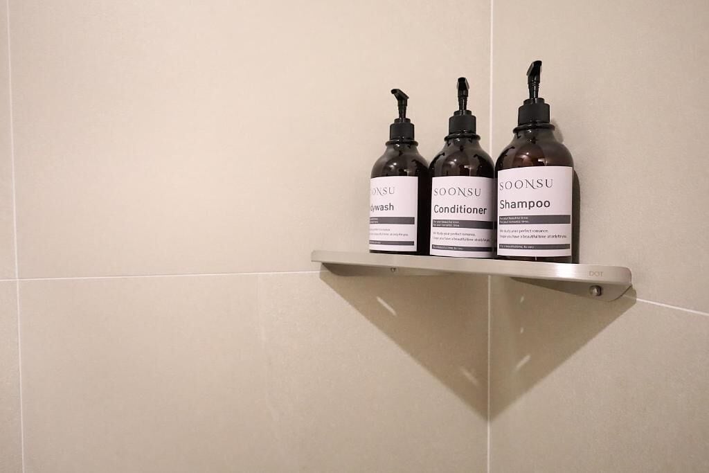 Uma prateleira no banheiro com três frascos de shower gel, condicionador e champô Soonsu.