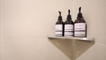 Uma prateleira no banheiro com três frascos de shower gel, condicionador e champô Soonsu.