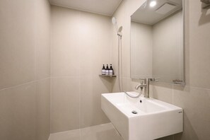 Casa de banho moderna com lavatório branco, chuveiro manual e prateleira com produtos de higiene pessoal.