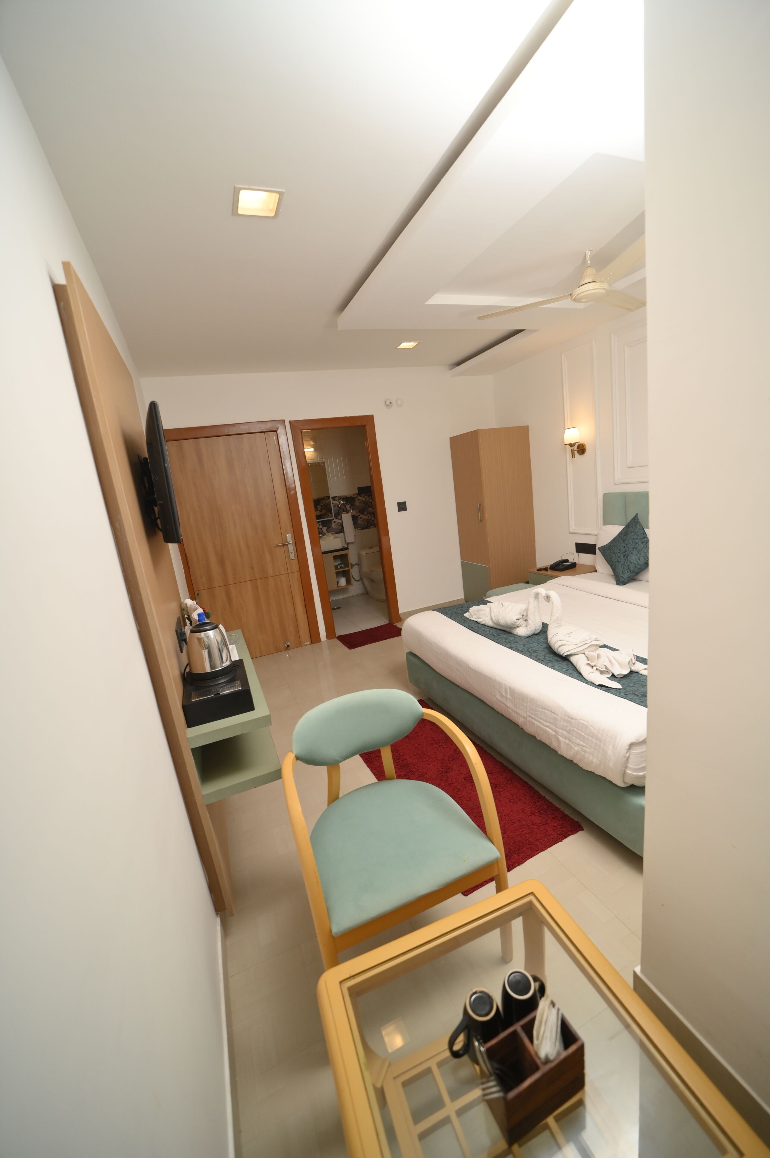 Quarto de hotel com cama, uma cadeira, uma mesinha com xícaras, televisão e guarda-roupa.
