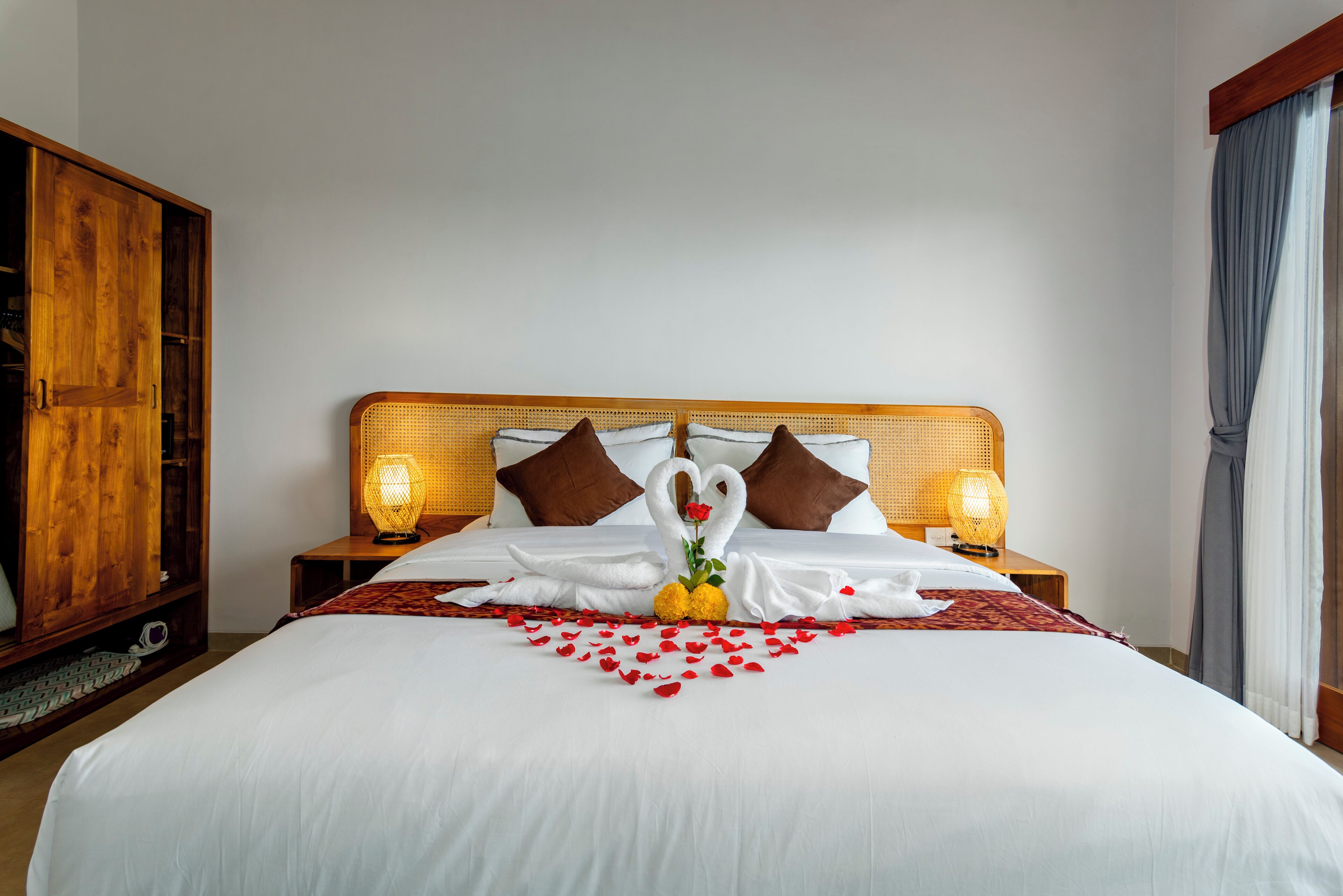 Uma cama bem arrumada com lençóis brancos, duas almofadas castanhas e um arranjo decorativo de toalhas e flores.