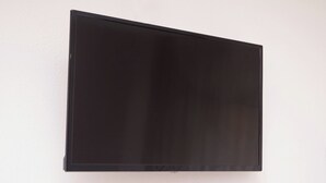 Um objeto preto fixado na parede, com superfície plana, possivelmente uma televisão ou monitor, em frente a uma parede lisa.
