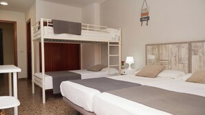 Quarto de hotel com beliches, uma escrivaninha e uma mesa de cabeceira com abajur.