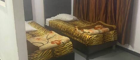 Quarto com duas camas, cada uma com colcha estampada, uma janela com cortinas e uma parede com padrões circulares.