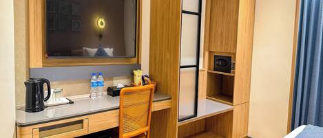Quarto de hotel com escrivaninha, cadeira, mini-geladeira, cama, guarda-roupa e espelho.