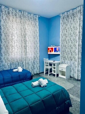 Quarto de hotel com duas camas, uma escrivaninha, uma cadeira e uma televisão.