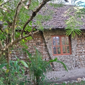 Um edifício rústico com telhado de palha, uma janela com venezianas de madeira e uma parede de pedra.