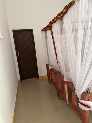 Quarto com cama de madeira com dossel, porta e piso de azulejos.