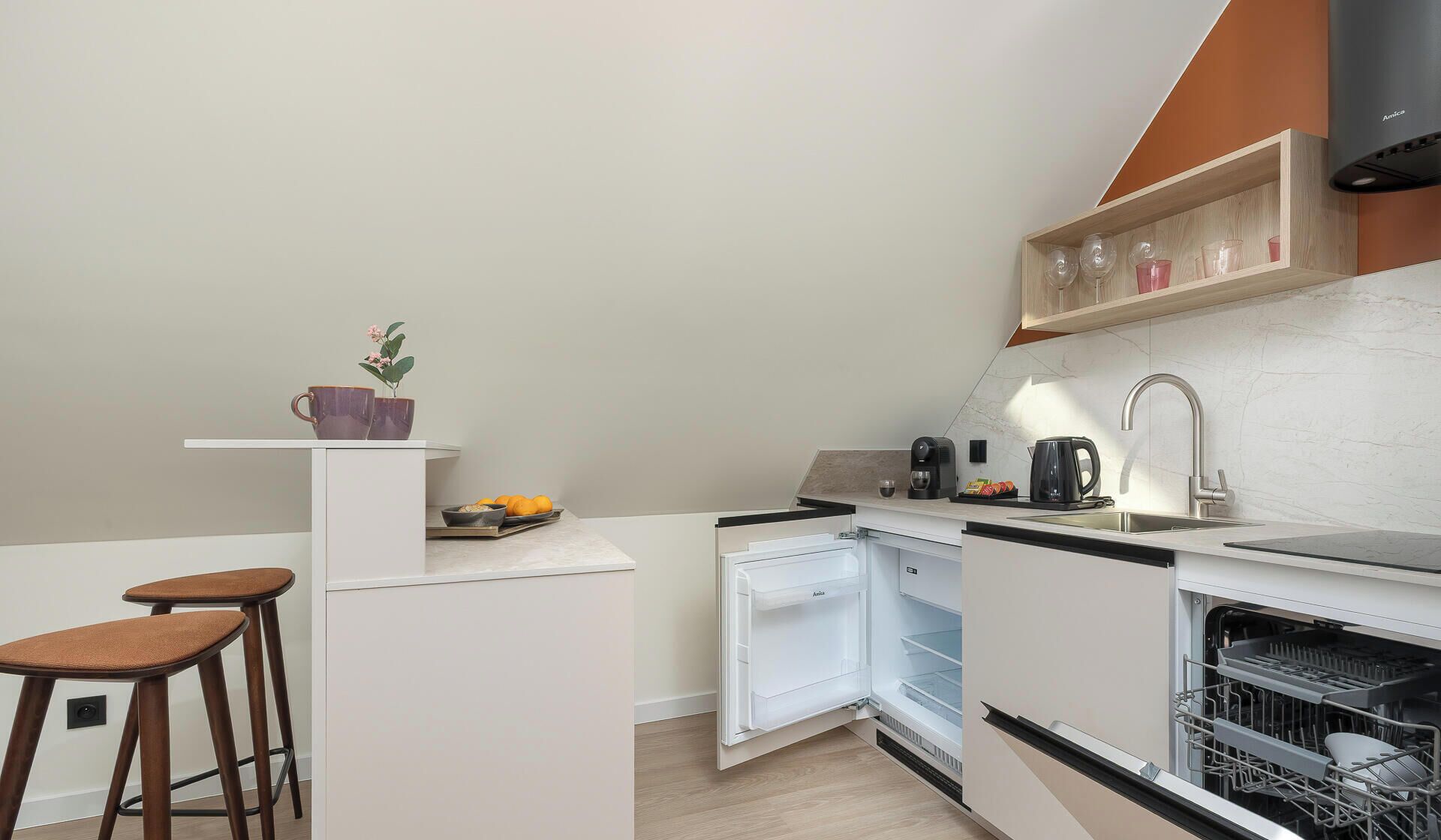 A compact kitchen with a built-in dishwasher, a coffee maker, and a kettle on the countertop.