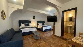 Quarto de hotel com duas camas, um sofá, uma televisão e uma casa de banho.