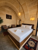 Quarto com uma cama grande, cabeceira de madeira, luminária pendente, mesa de cabeceira, uma cadeira, um espelho e um tapete.