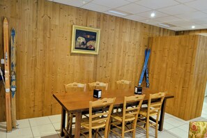 Um quarto com painéis de madeira, uma mesa de jantar e cadeiras, um quadro na parede e esquis encostados.