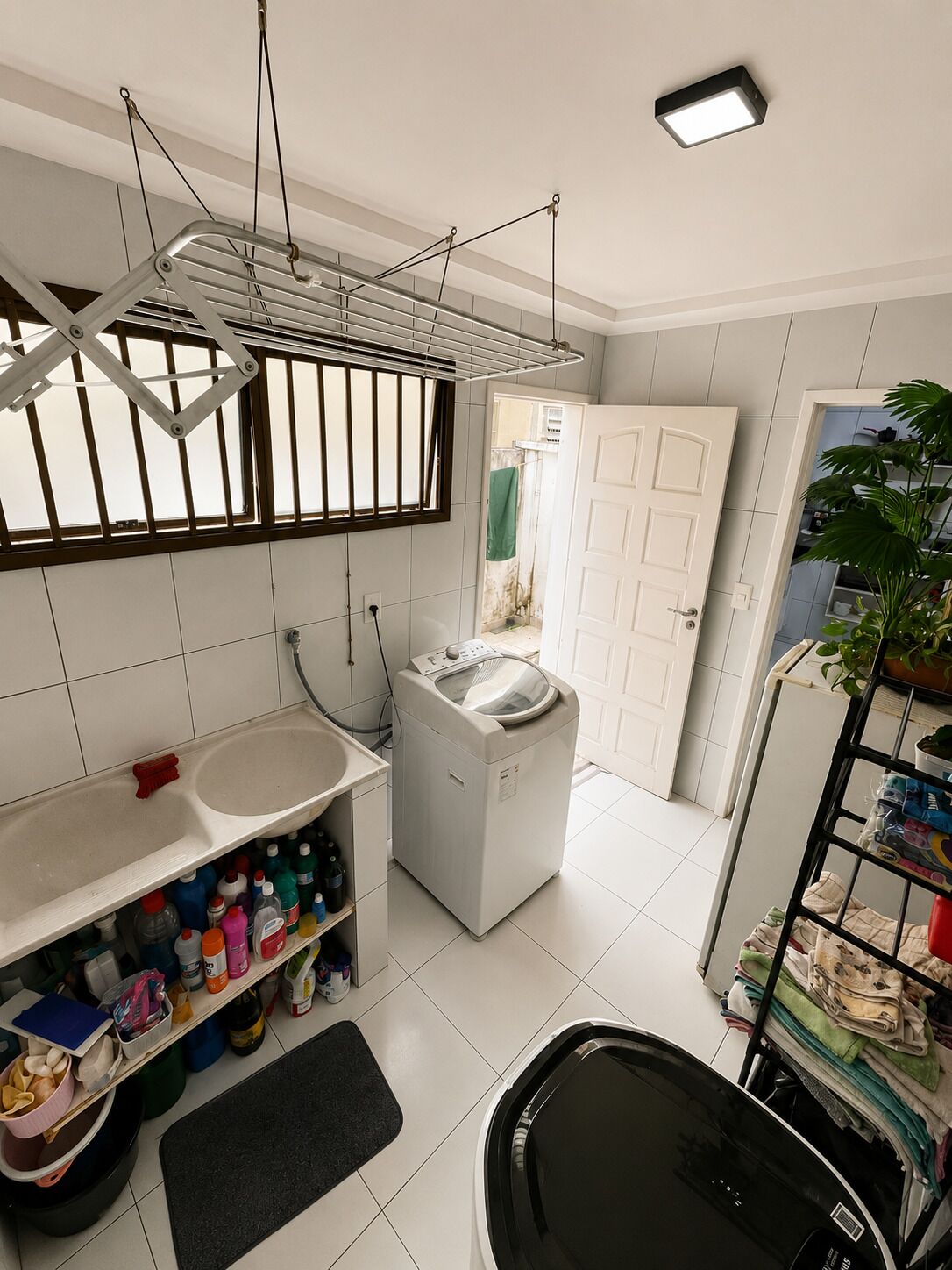 Casa de banho compacta e moderna, com máquina de lavar embutida, lavatório com vários artigos de higiene e um varal.