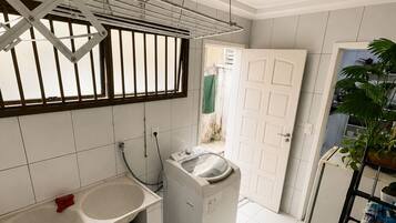 Casa de banho compacta e moderna, com máquina de lavar embutida, lavatório com vários artigos de higiene e um varal.
