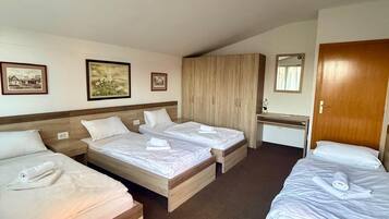 Quarto de hotel com três camas de solteiro, um guarda-roupa de madeira, uma secretária com cadeira e quadros nas paredes.