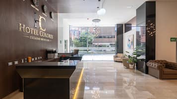 Uma área de recepção de hotel com design moderno, incluindo um balcão de atendimento, espaço de estar e grandes janelas com vista para a cidade.