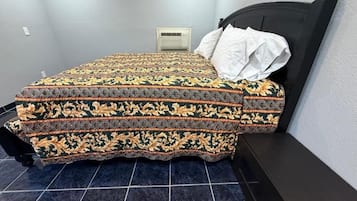 Uma cama com colcha estampada, travesseiro branco e cabeceira preta em um quarto com piso de azulejos.