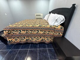 Uma cama com colcha estampada, travesseiro branco e cabeceira preta em um quarto com piso de azulejos.