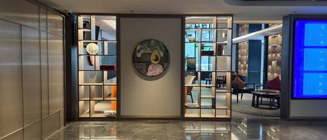 Um hall de hotel moderno com piso refletivo, uma obra de arte central e uma área de estar com mesas e cadeiras.
