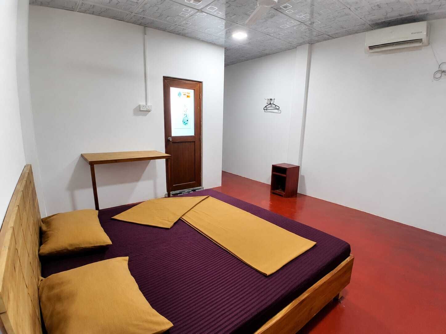 Um quarto com uma cama, uma mesinha, uma porta e um aparelho de ar condicionado.