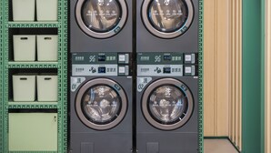 Quatro máquinas de lavar roupa frontais idênticas, dispostas lado a lado, com ecrãs digitais.