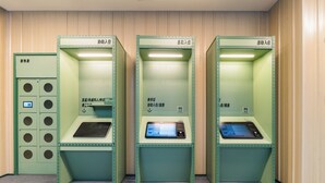 Uma fileira de totens de autoatendimento com interfaces digitais, cada um identificado com caracteres chineses, em um ambiente com painéis de madeira e carpete listrado.
