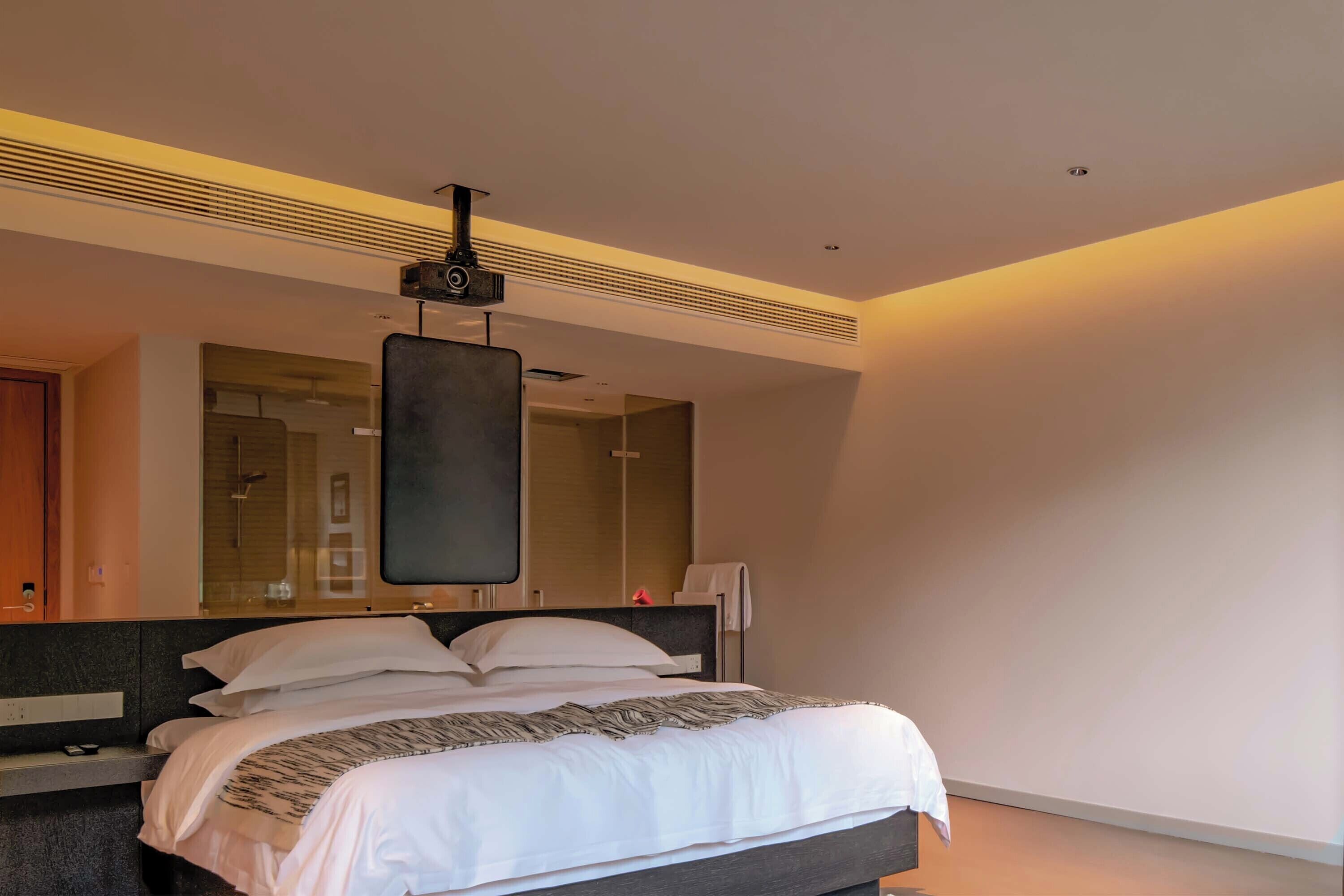Quarto moderno com cama grande, mesa de cabeceira, espelho e luminária no teto.
