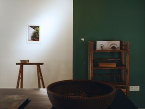 Um quarto com um cavalete de madeira, um quadro na parede, uma parede verde e uma estante com objetos decorativos.