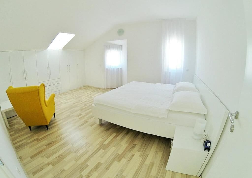 Quarto com cama, uma cadeira amarela, guarda-roupa e clarabóia.