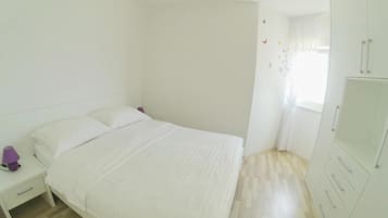 Um quarto com uma cama, mesa de cabeceira, guarda-roupa e janela com cortinas.