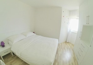 Um quarto com uma cama, mesa de cabeceira, guarda-roupa e janela com cortinas.