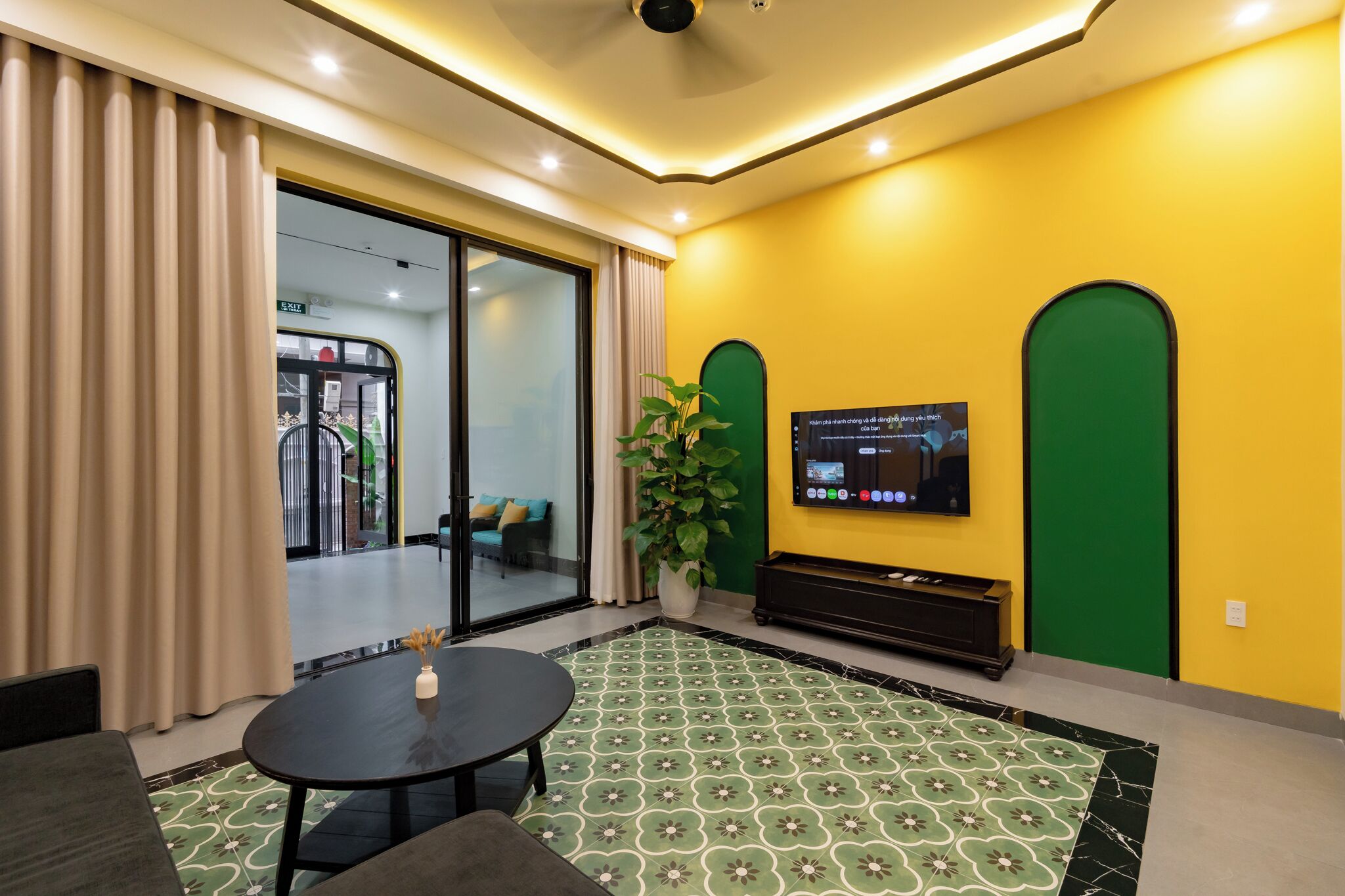 Uma sala de estar moderna com uma televisão grande, um sofá, uma mesa de centro e uma porta de vidro deslizante que dá para uma varanda.