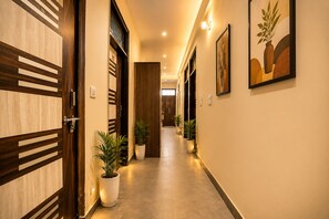 Um corredor com portas de madeira, plantas em vasos e quadros nas paredes.