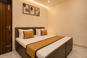 Quarto de hotel com uma cama, uma porta de madeira e três obras de arte com folhas emolduradas na parede.