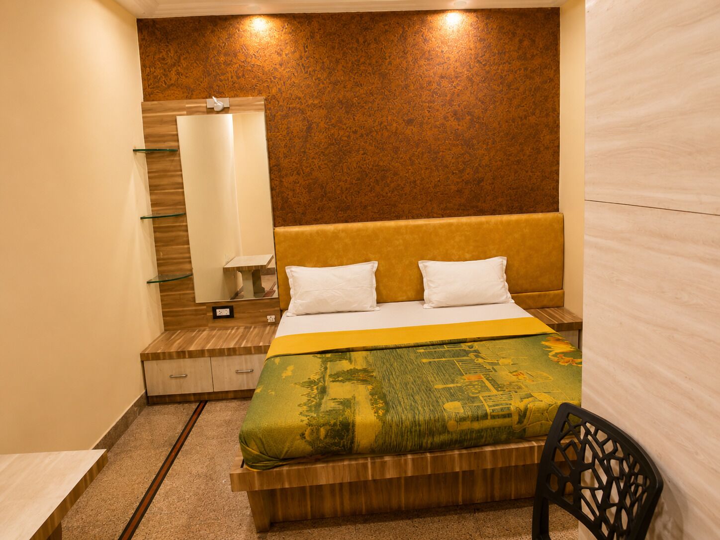 Quarto de hotel com uma cama, uma mesa de cabeceira, um espelho e uma cadeira.