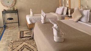 Quarto de hotel com duas camas, um espelho redondo, uma mesinha com um banquinho e um tapete estampado.