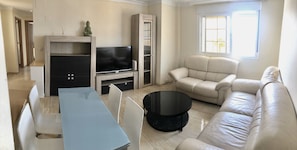 Uma sala de estar com sofá, televisão, mesa de centro e mesa de jantar.