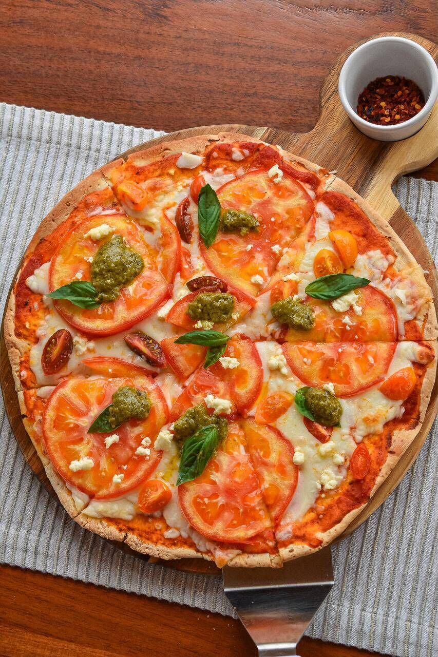 Pizza com rodelas de tomate, queijo e manjericão sobre uma tábua de madeira.